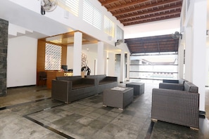 Um hall espaçoso com balcão de recepção, móveis de vime e vista para a área da piscina.
