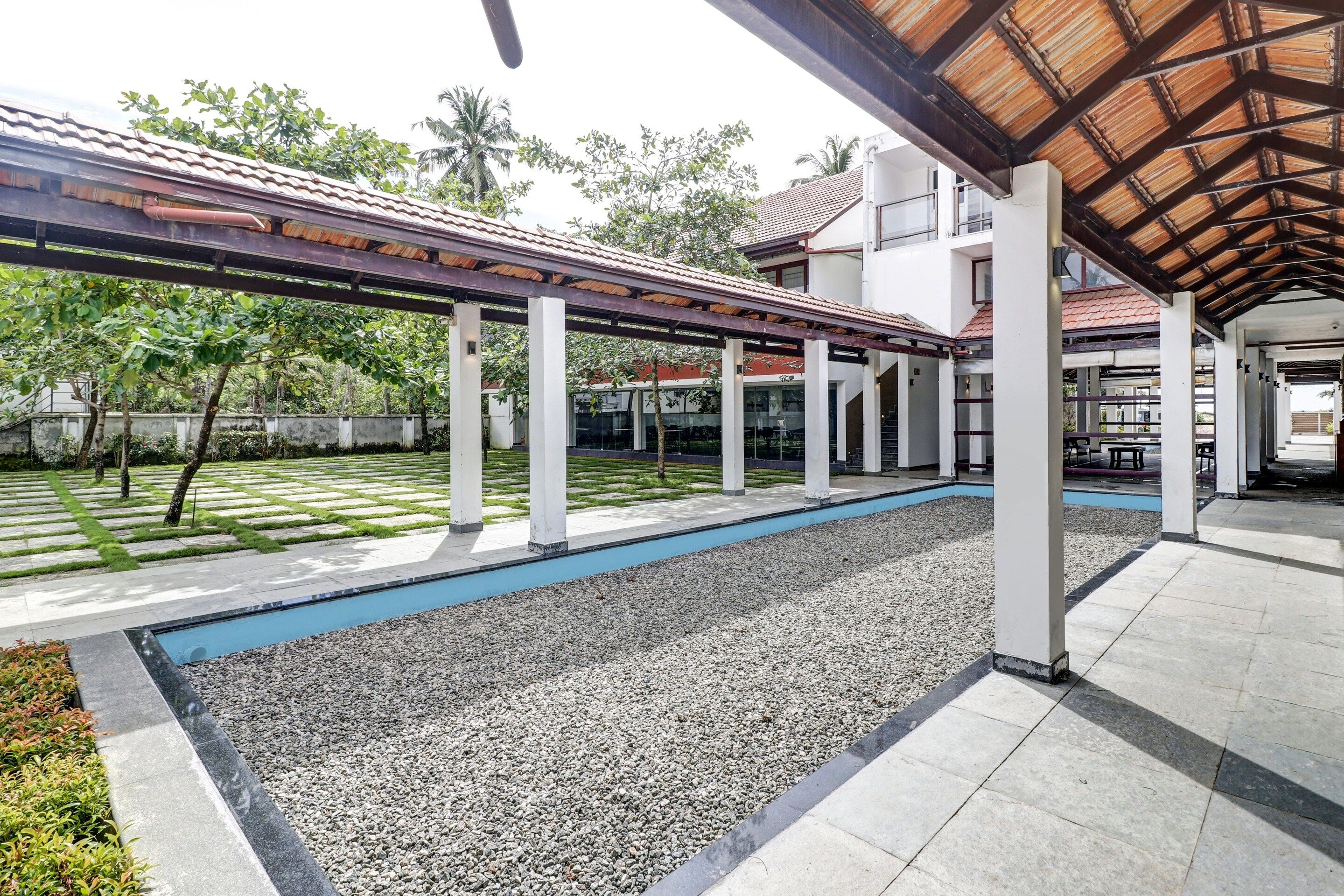Uma área externa coberta com piscina, rodeada por um jardim com grama bem aparada e árvores.