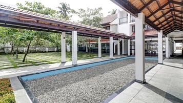 Uma área externa coberta com piscina, rodeada por um jardim com grama bem aparada e árvores.