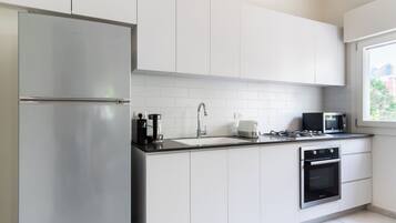 Cozinha moderna com armários brancos, eletrodomésticos de aço inoxidável e janela que ilumina naturalmente o espaço.