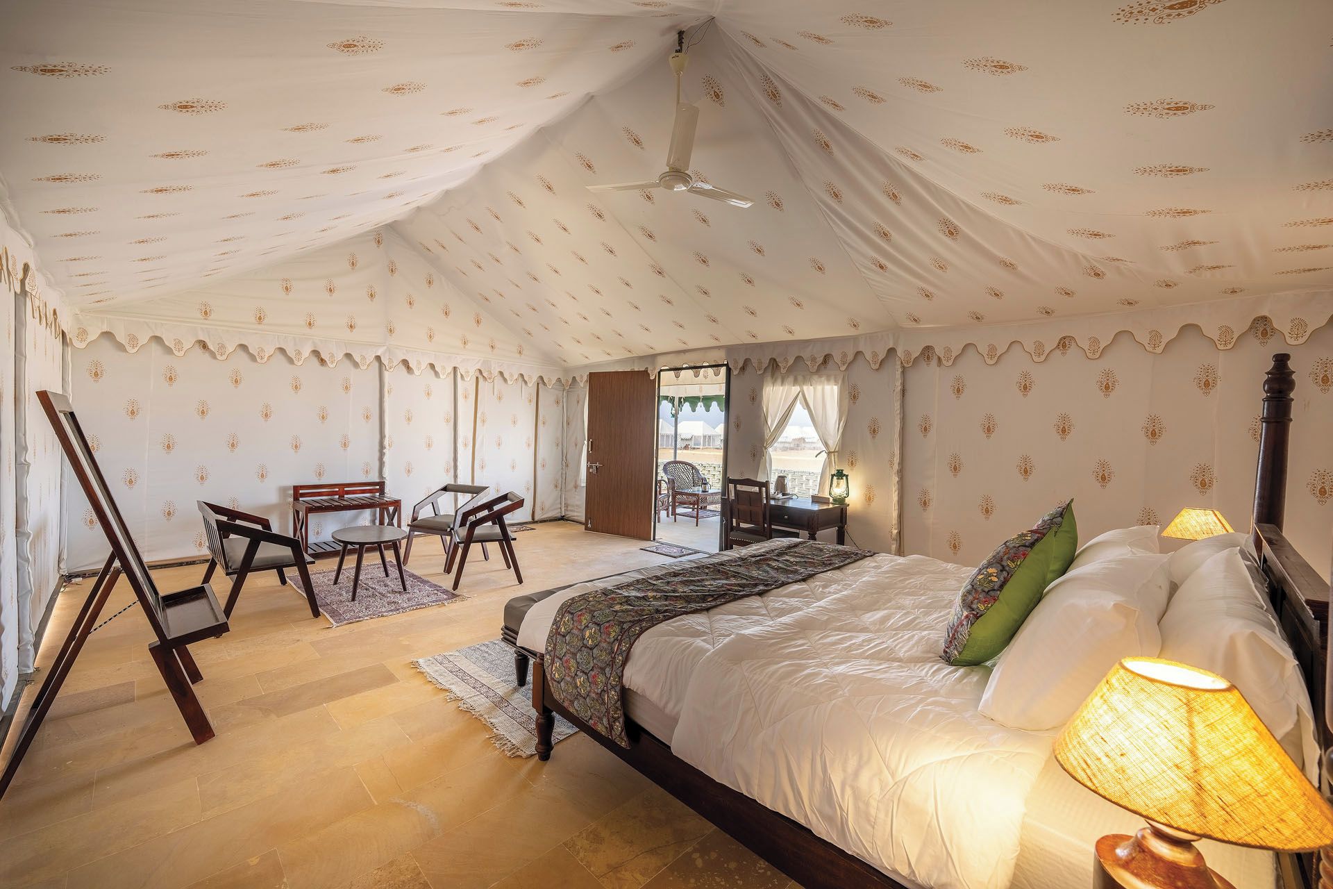 Quarto tipo tenda com uma cama, uma mesa e cadeiras, e um ventilador de teto.