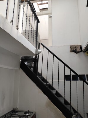 Escadaria com corrimão preto e paredes brancas, que dá acesso a um andar superior.