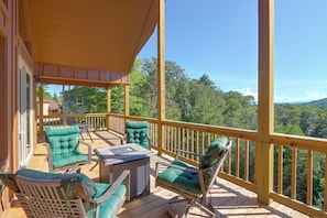 Um deck de madeira com mobiliário externo, incluindo cadeiras e uma mesa, com vista para uma paisagem arborizada.