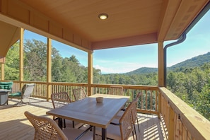 Um deck de madeira com mesa e cadeiras, com vista para uma paisagem arborizada.
