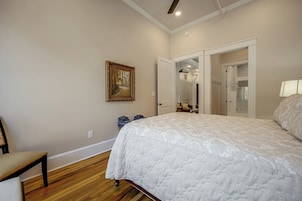 Quarto com uma cama grande, uma cadeira, um quadro e um banheiro visível por uma porta aberta.