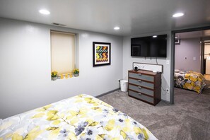 Quarto com duas camas, penteadeira, televisão e janela com persianas.