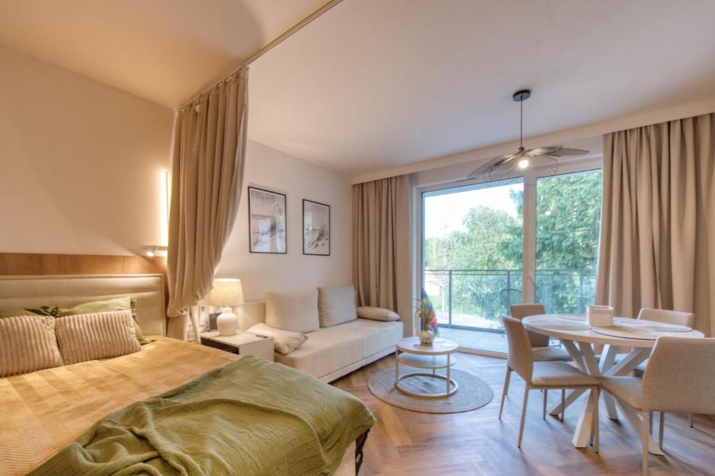 Quarto de hotel com cama, sofá, mesa de jantar com cadeiras, varanda com cortinas e ventilador de teto.
