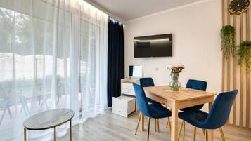 Uma sala de jantar moderna com mesa de madeira, cadeiras azuis, televisão de tela plana e janela com cortinas leves.