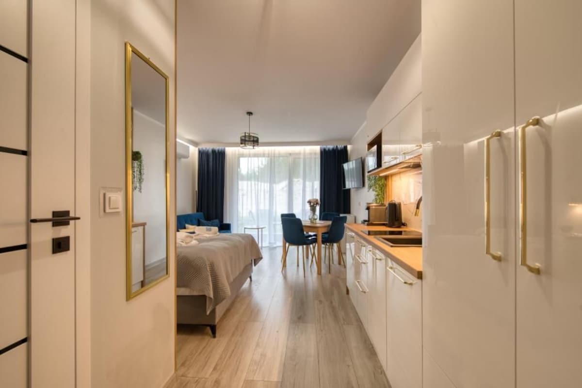 Quarto de hotel moderno com cama, área de refeições e cozinha compacta.