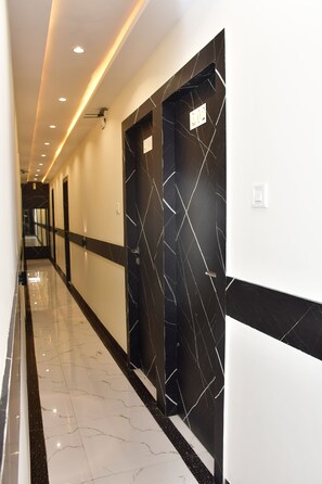 Corredor de hotel com piso de mármore, paredes em preto e branco e portas com números de quarto.