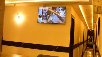 Um hall de hotel com um candelabro, uma TV de tela plana, um sofá verde e piso de mármore.