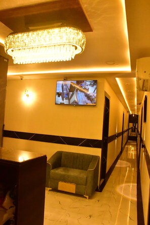 Um hall de hotel com um candelabro, uma TV de tela plana, um sofá verde e piso de mármore.