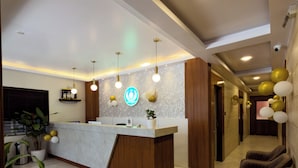 Uma área de recepção com piso de mármore, balcão de madeira, uma planta e um balcão de atendimento com um letreiro de neon.