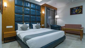 Quarto de hotel com uma cama grande, área de estar com sofá e poltrona, um quadro na parede e um ventilador de teto.