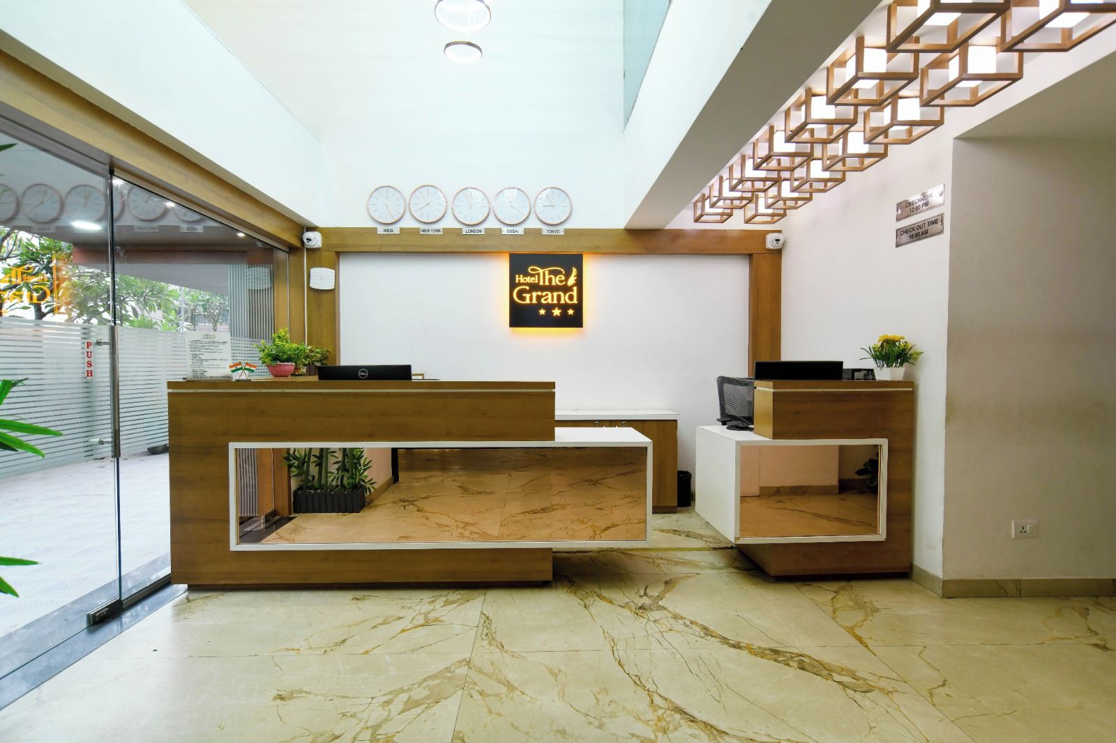 Área de recepção de hotel com balcão, placa indicando 'Hotel Grand' e relógio fixado na parede.