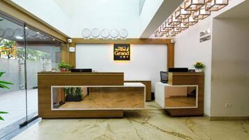 Área de recepção de hotel com balcão, placa indicando 'Hotel Grand' e relógio fixado na parede.