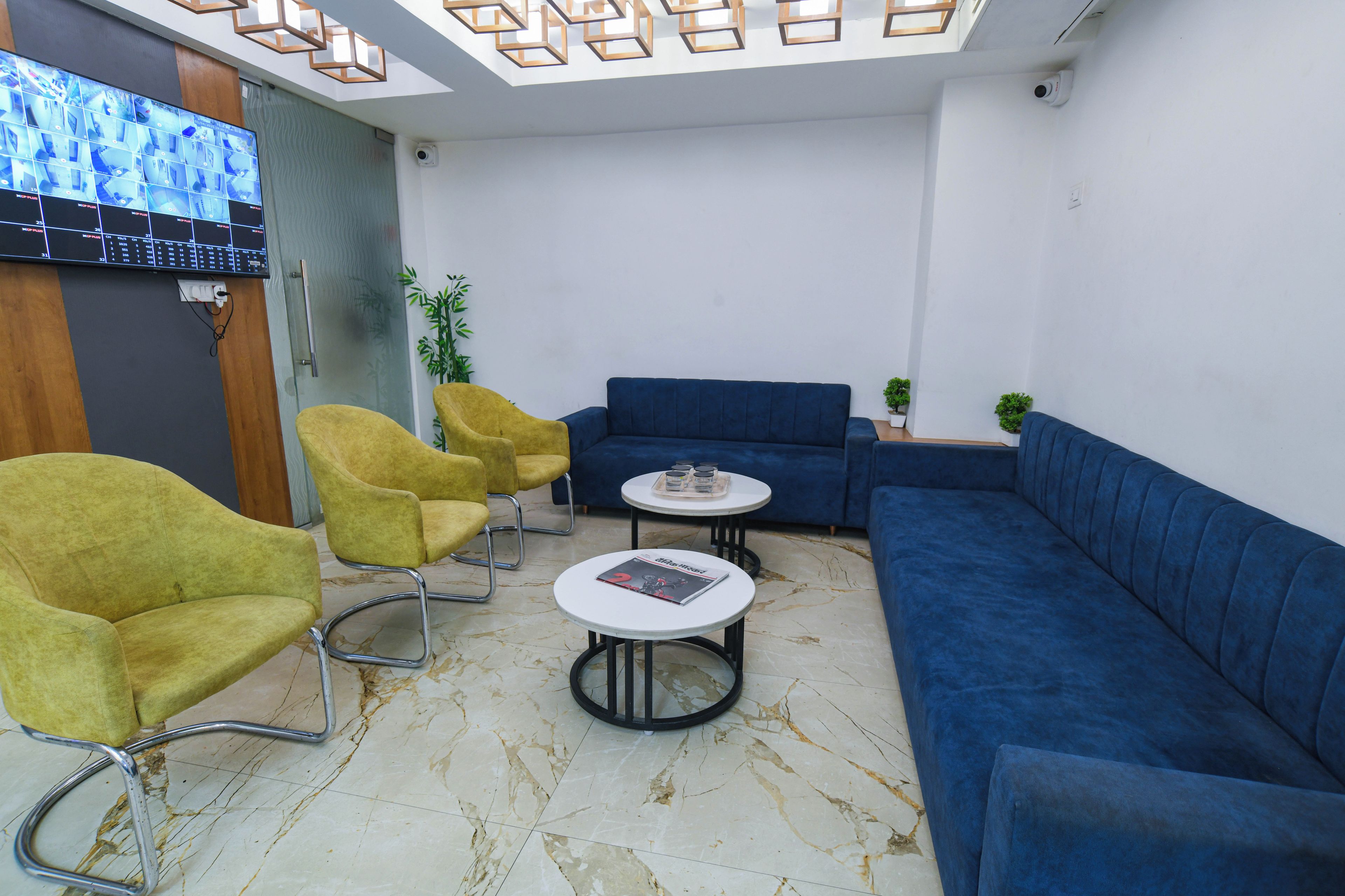 Uma área de espera moderna com cadeiras amarelas, um sofá azul e uma pequena mesa com revistas.