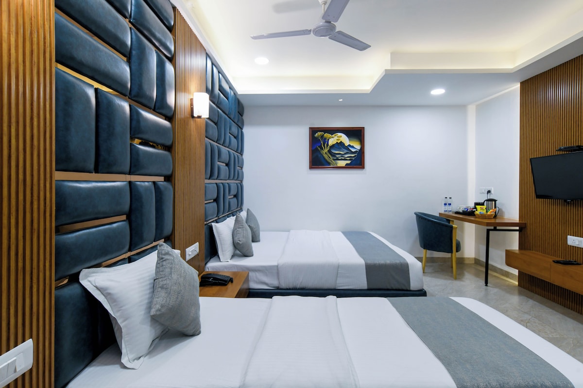 Quarto de hotel com duas camas, uma escrivaninha, televisão e ventoinha no teto.