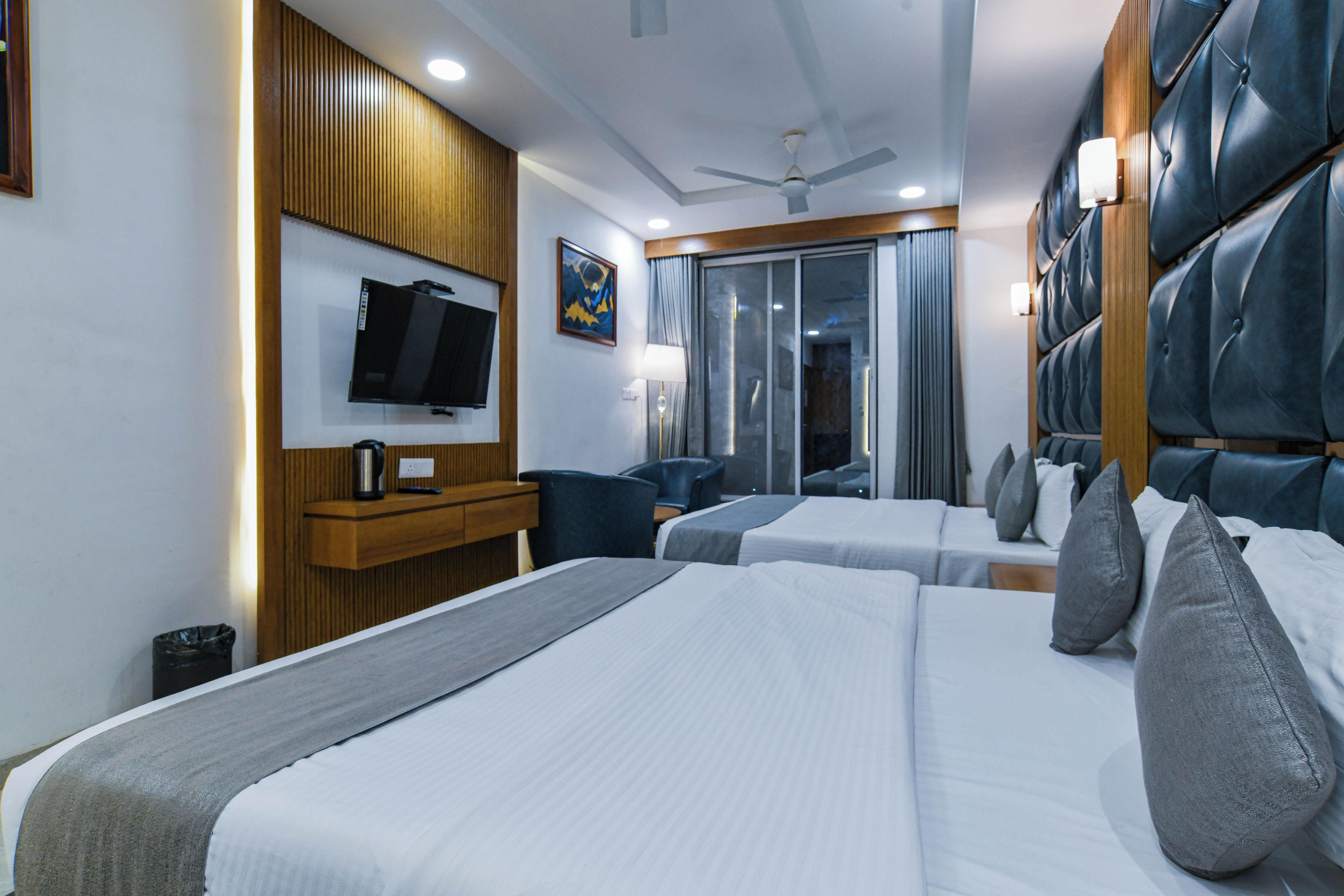 Quarto de hotel com duas camas, televisão, escrivaninha com cafeteira e janela com cortinas.