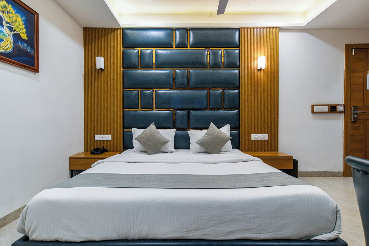 Quarto de hotel com uma cama grande, cabeceira de madeira, abajures e um quadro na parede.