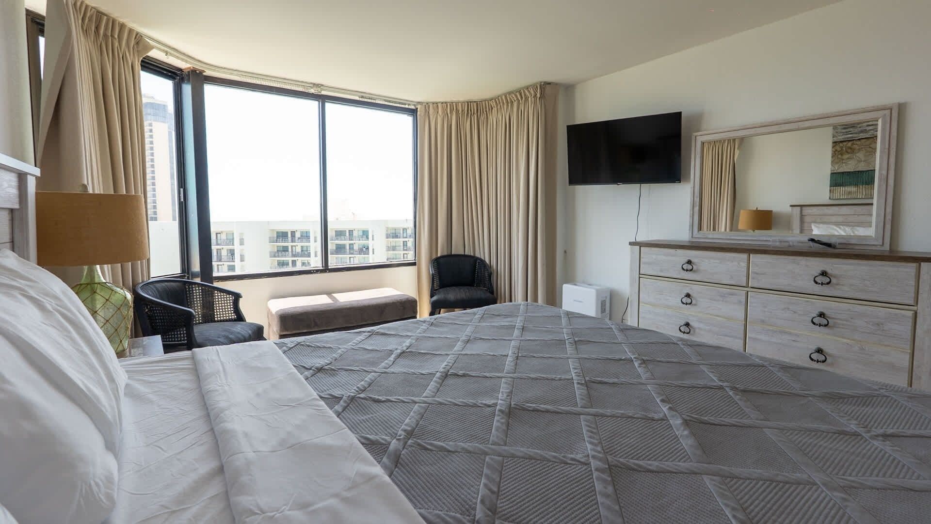 Quarto de hotel com uma cama grande, televisão de tela plana, cômoda e uma cadeira.