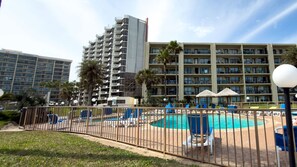 Um hotel com piscina, várias varandas e palmeiras.