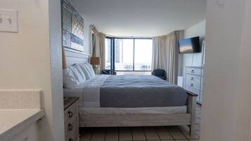 Quarto de hotel com cama, televisão, escrivaninha e janela com cortinas.