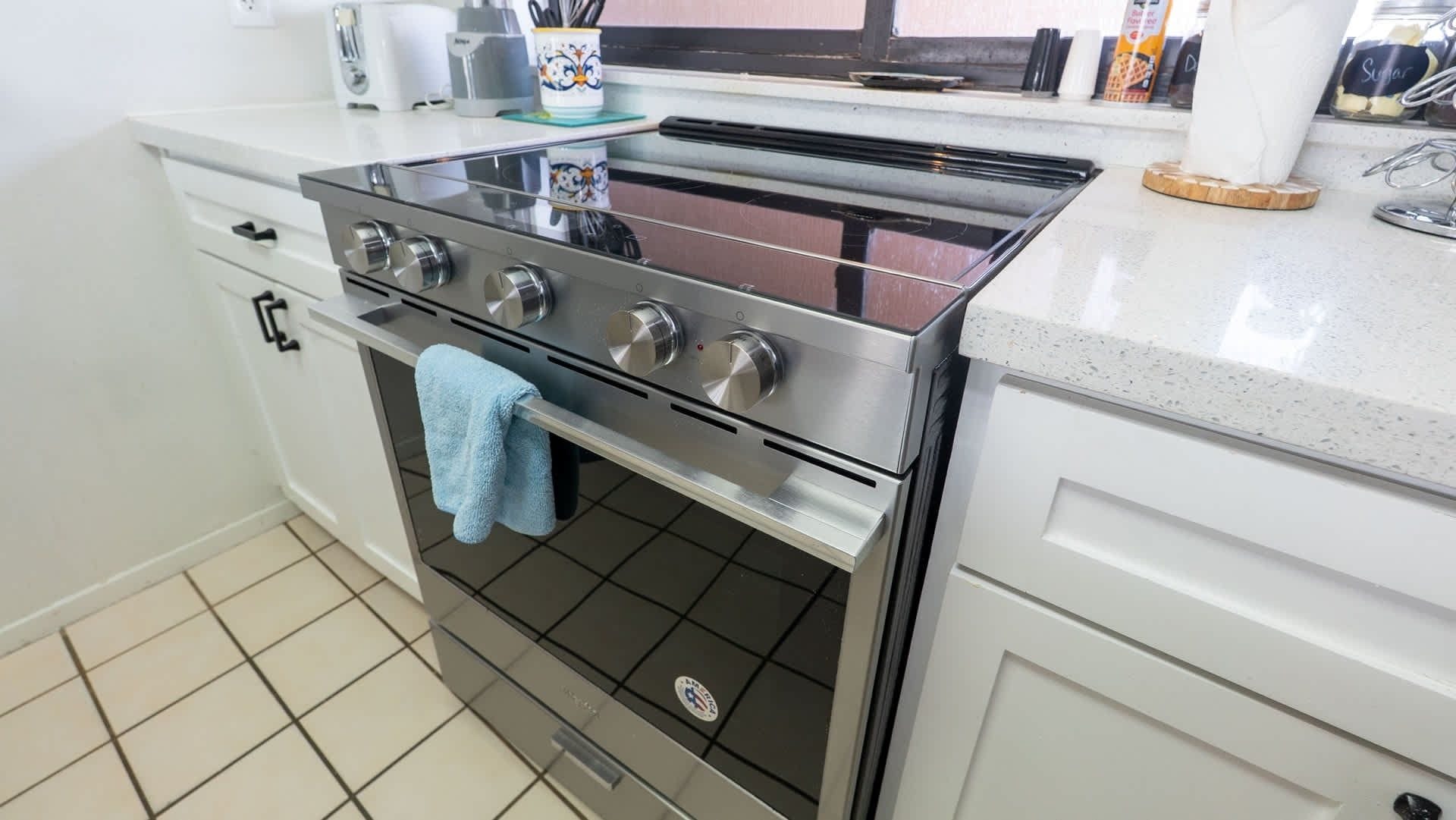 Cozinha com fogão de aço inoxidável, bancada branca e chão de azulejos.