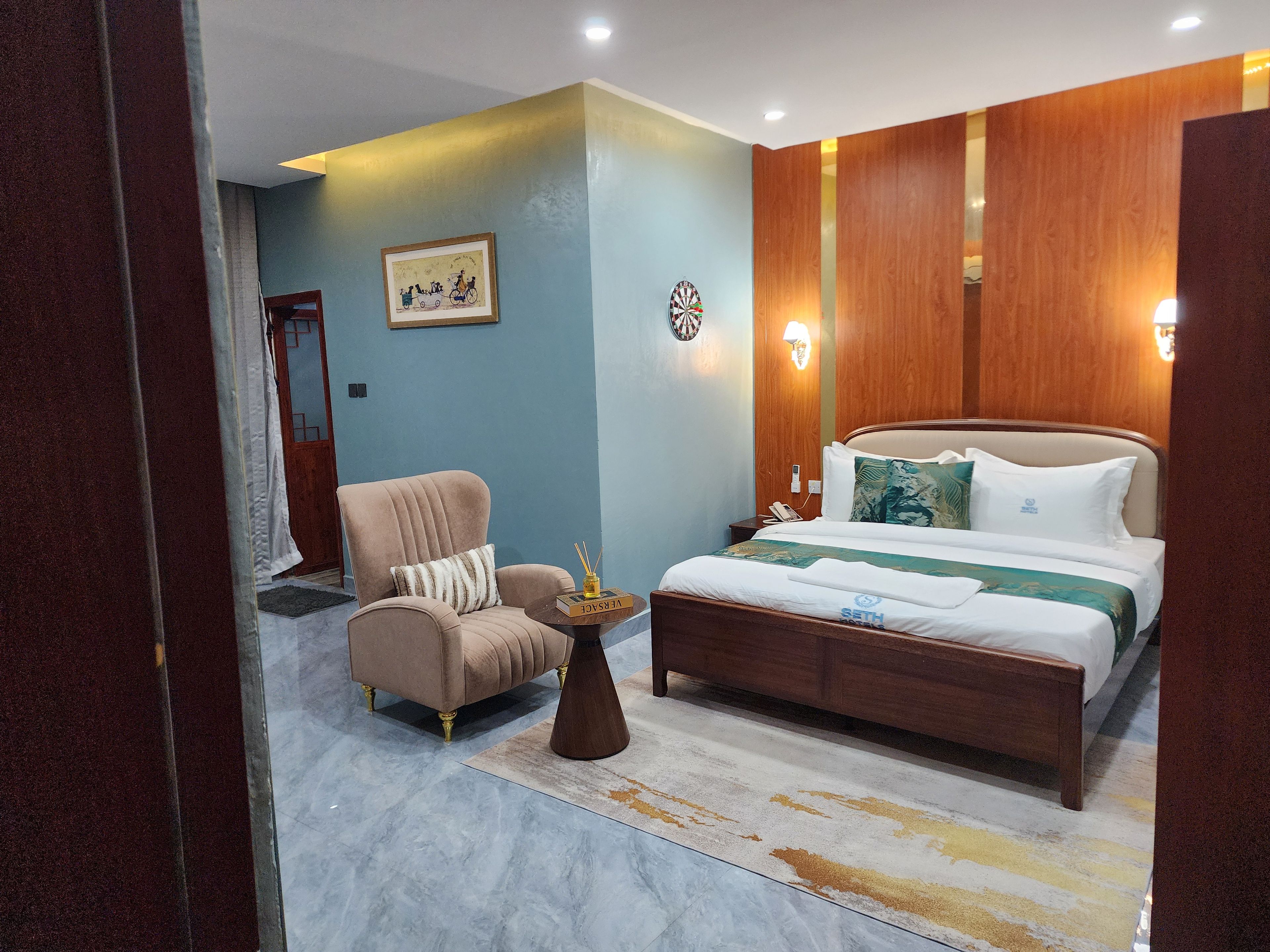 Quarto de hotel com cama, cadeira, mesa de cabeceira e luminária fixada na parede.