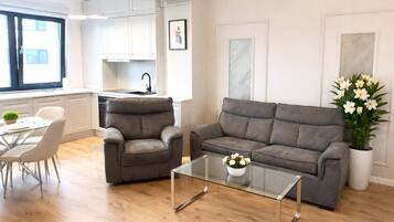 Uma sala de estar moderna com sofá, poltrona, mesa de centro de vidro e um espaço de refeições com cadeiras e mesa.