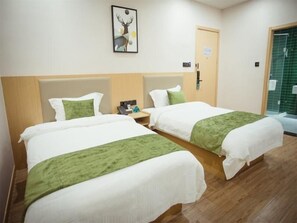 Quarto de hotel com duas camas, cabeceira de madeira, manta verde, telefone e porta com toalha pendurada.