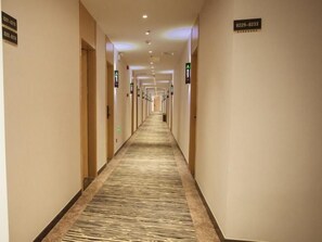 Corredor de hotel com piso em carpete, portas em ambos os lados e placas de sinalização.