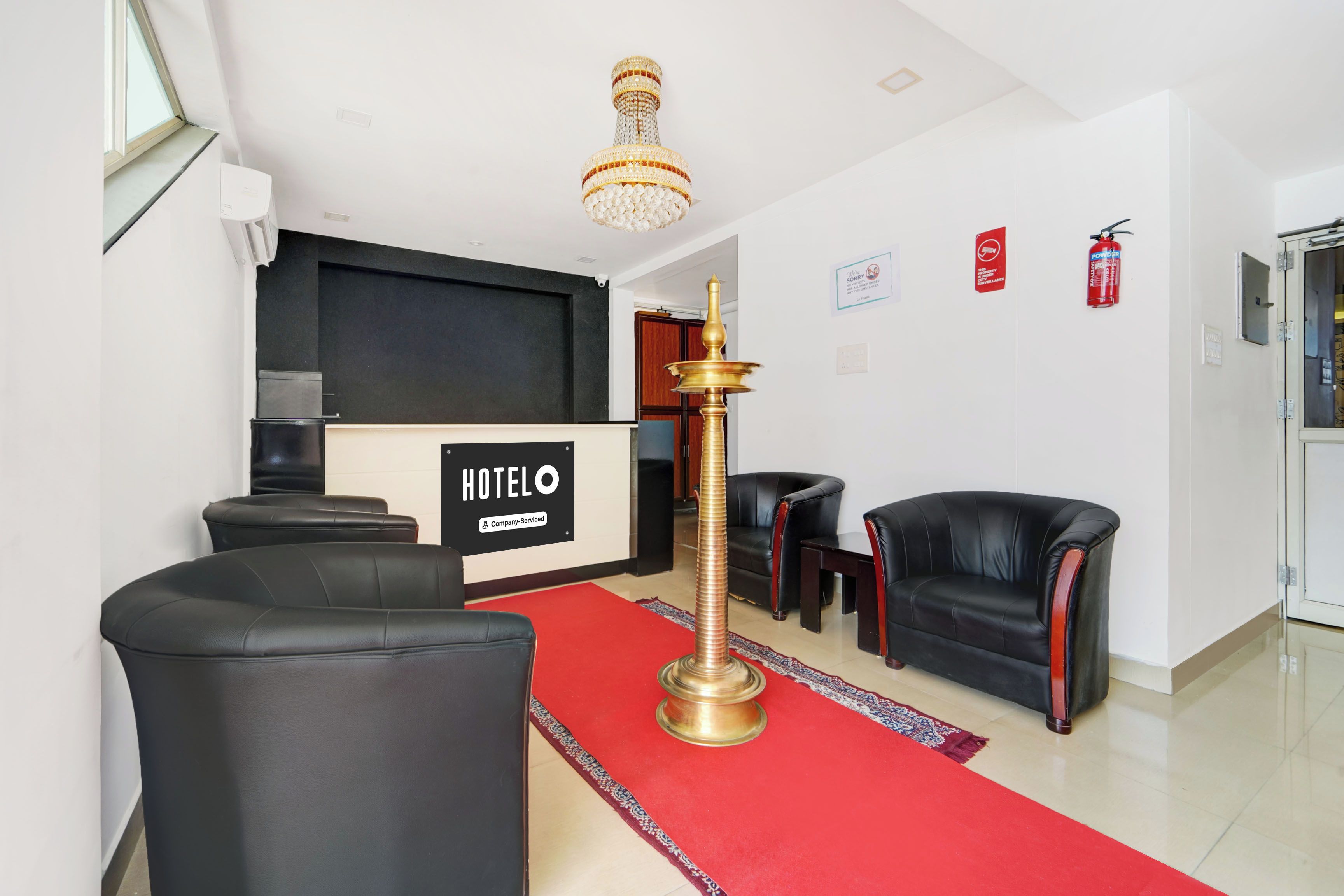 Uma área de recepção de hotel com balcão, sofás de couro preto, tapete vermelho e um candelabro.