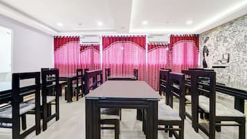 Uma sala de jantar com uma mesa comprida e cadeiras, cortinas vermelhas estampadas e uma parede com ilustrações de comida.