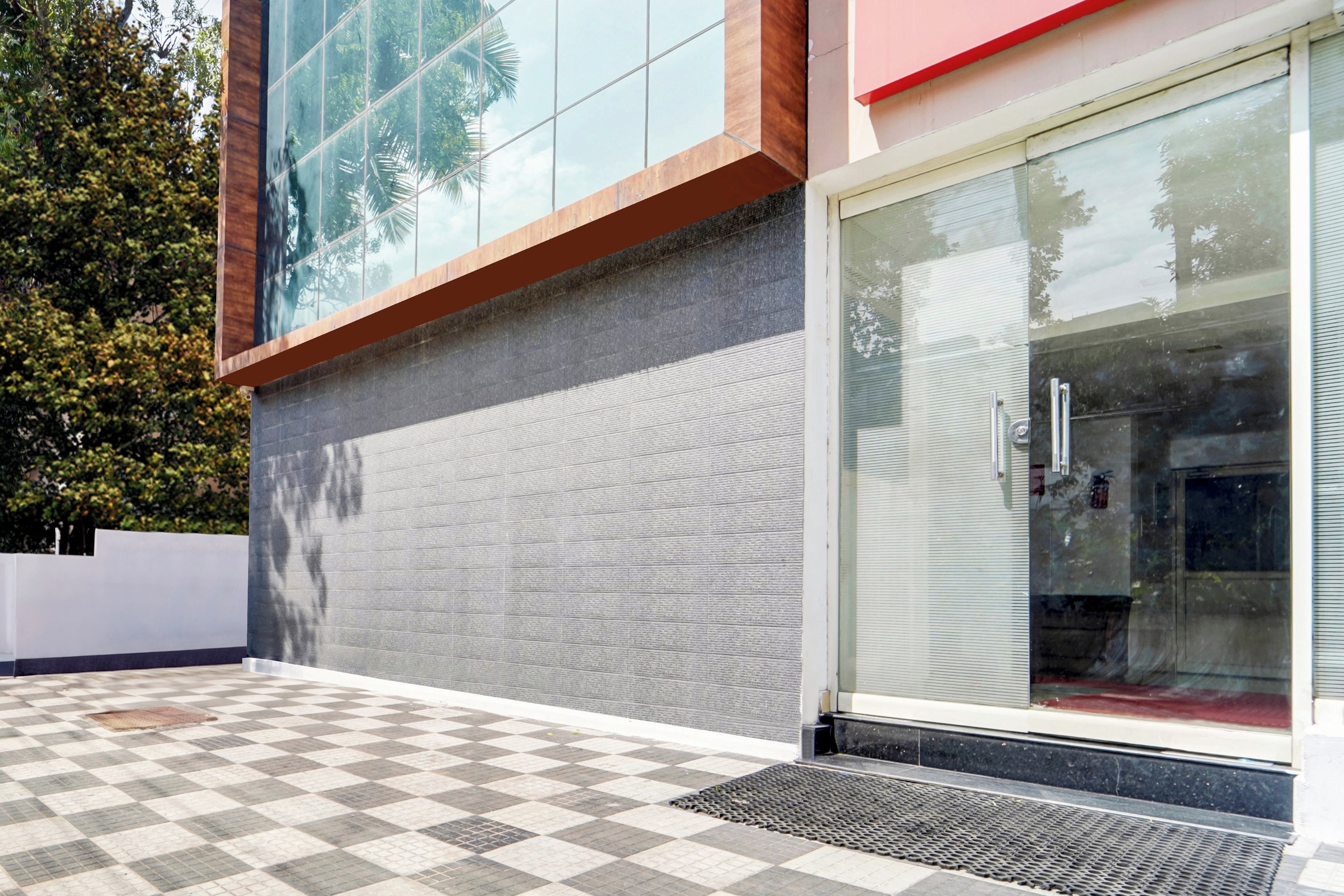 Entrada de um edifício com piso xadrez, porta de vidro e toldo vermelho.