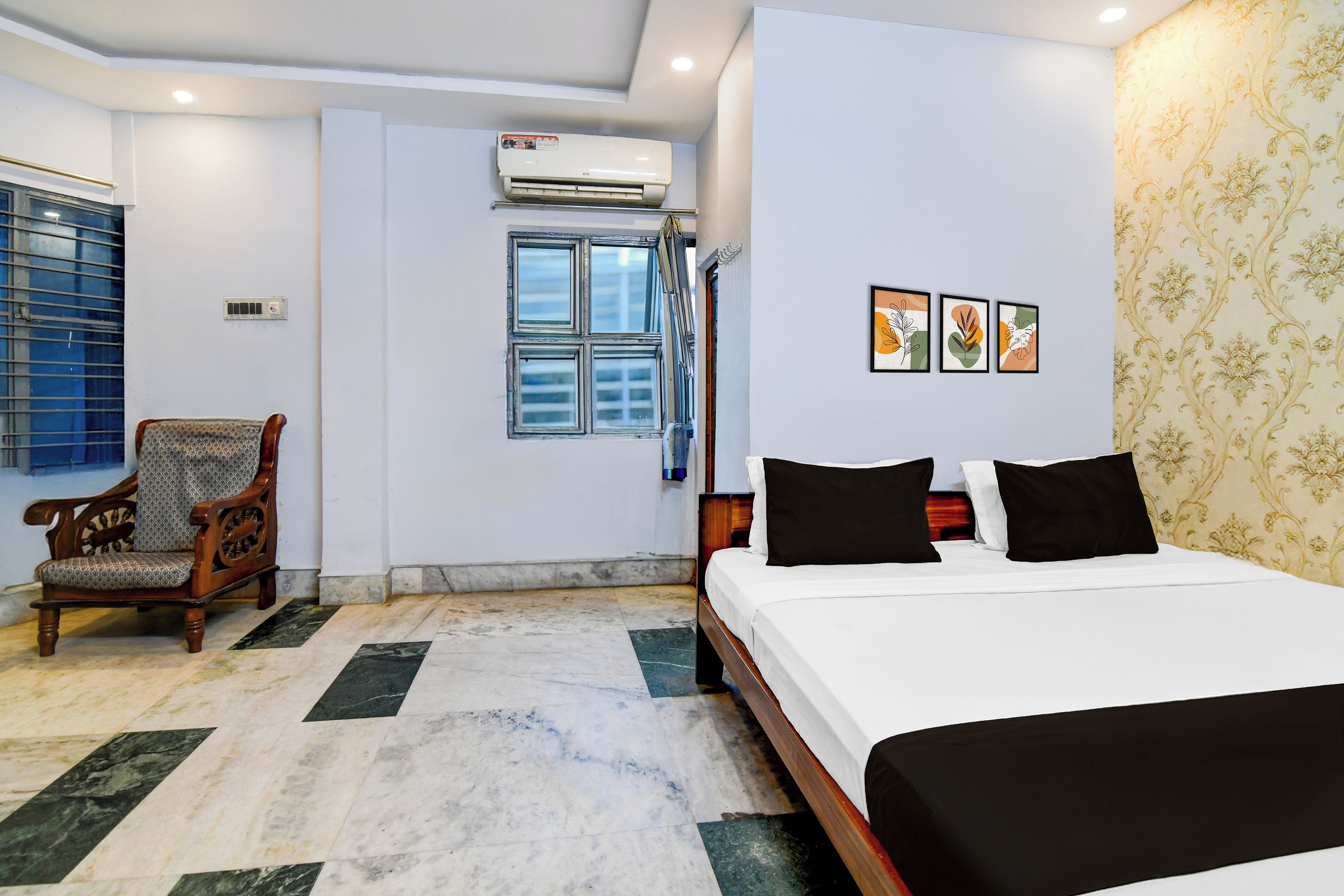 Quarto de hotel com cama, uma cadeira, uma janela e parede com três quadros.