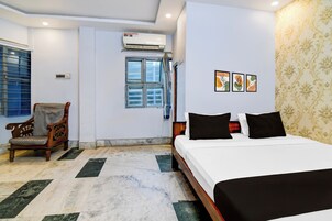 Quarto de hotel com cama, uma cadeira, uma janela e parede com três quadros.