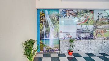 Uma área de recepção com piso xadrez, um mural grande com diversas cenas e duas plantas em vasos.