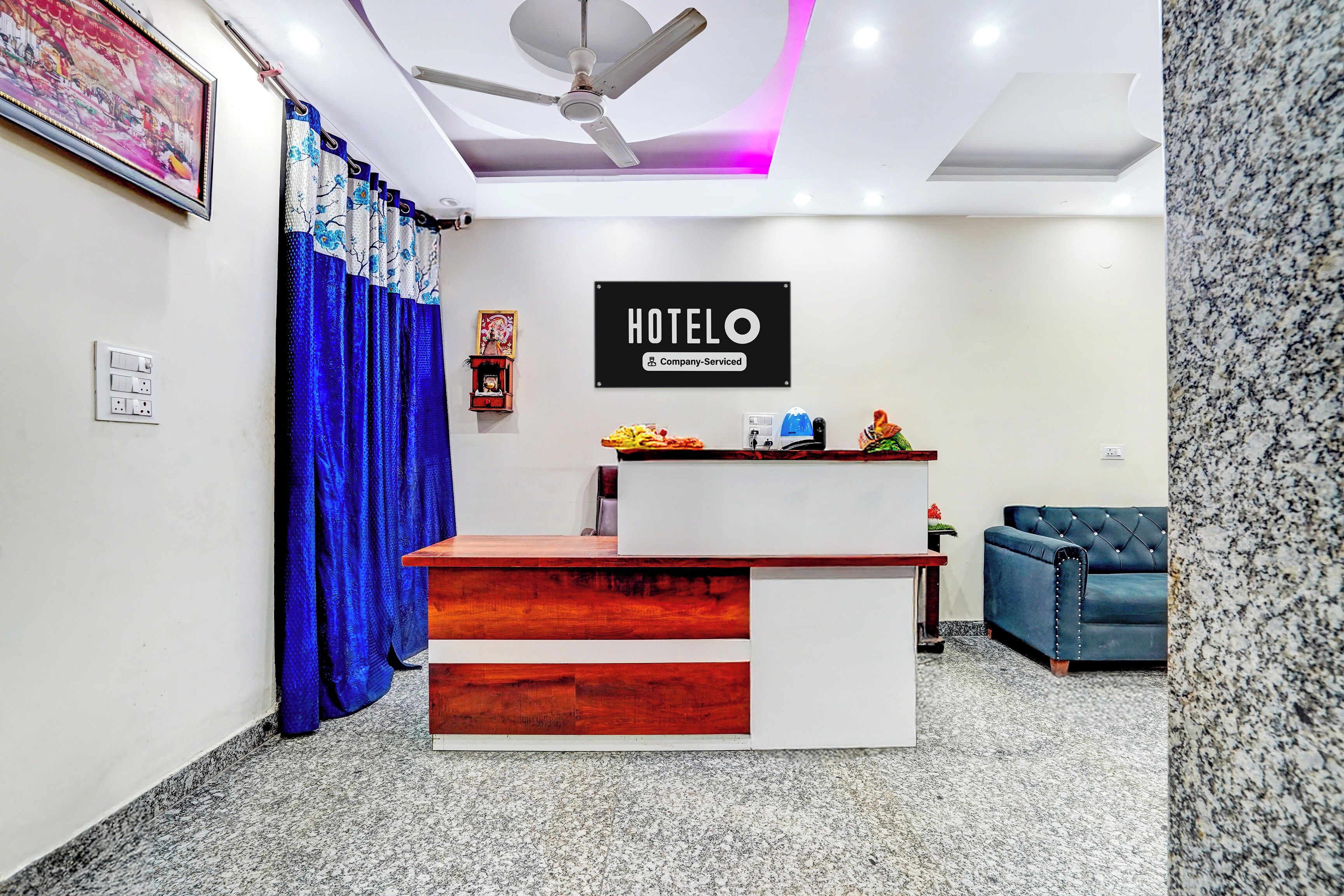 Uma área de recepção de hotel com design moderno, incluindo um balcão de atendimento, um ventilador de teto e uma placa indicando que o hotel é de serviço corporativo.