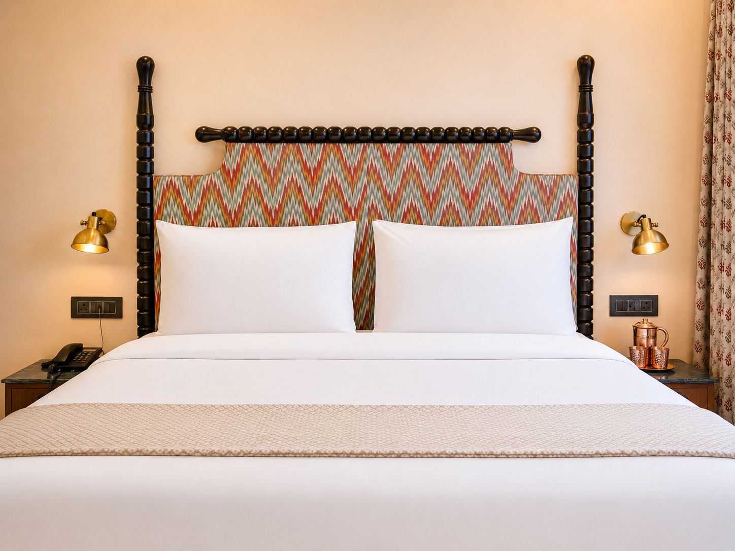 Quarto de hotel com cama de dossel, duas luminárias de cabeceira, telefone e painel decorativo na parede.