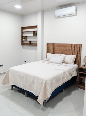 Quarto com cama, cabeceira de madeira, prateleira na parede e aparelho de ar condicionado.