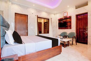 Quarto de hotel com cama, escrivaninha, cadeira, TV fixada na parede e guarda-roupa de madeira.