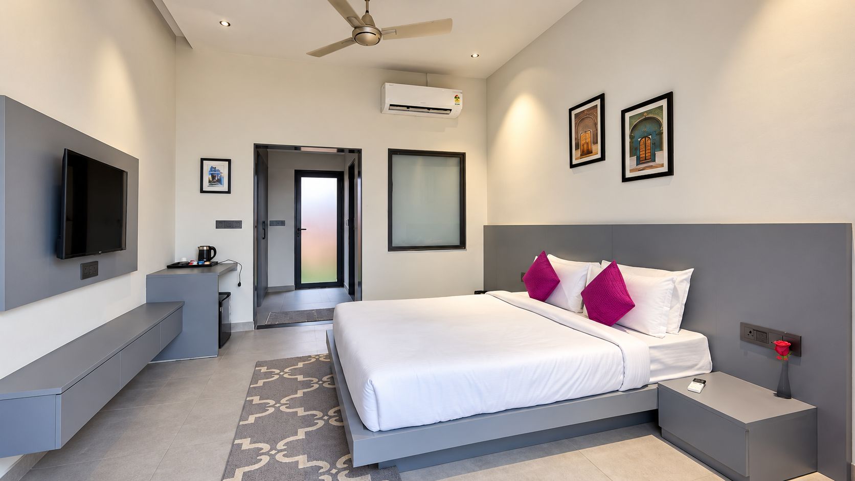 Quarto de hotel moderno com cama, mesa de cabeceira, televisão e escrivaninha com cadeira.