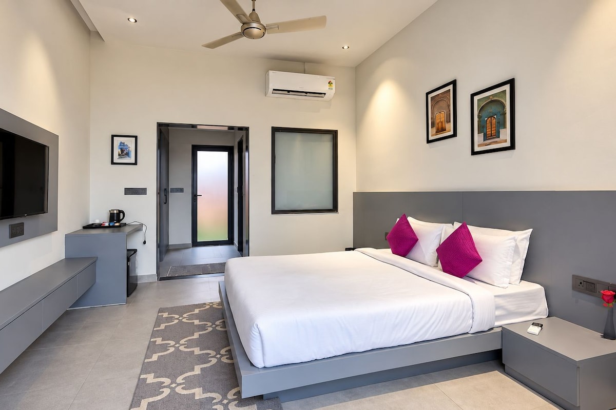 Quarto de hotel moderno com cama, mesa de cabeceira, televisão e escrivaninha com cadeira.