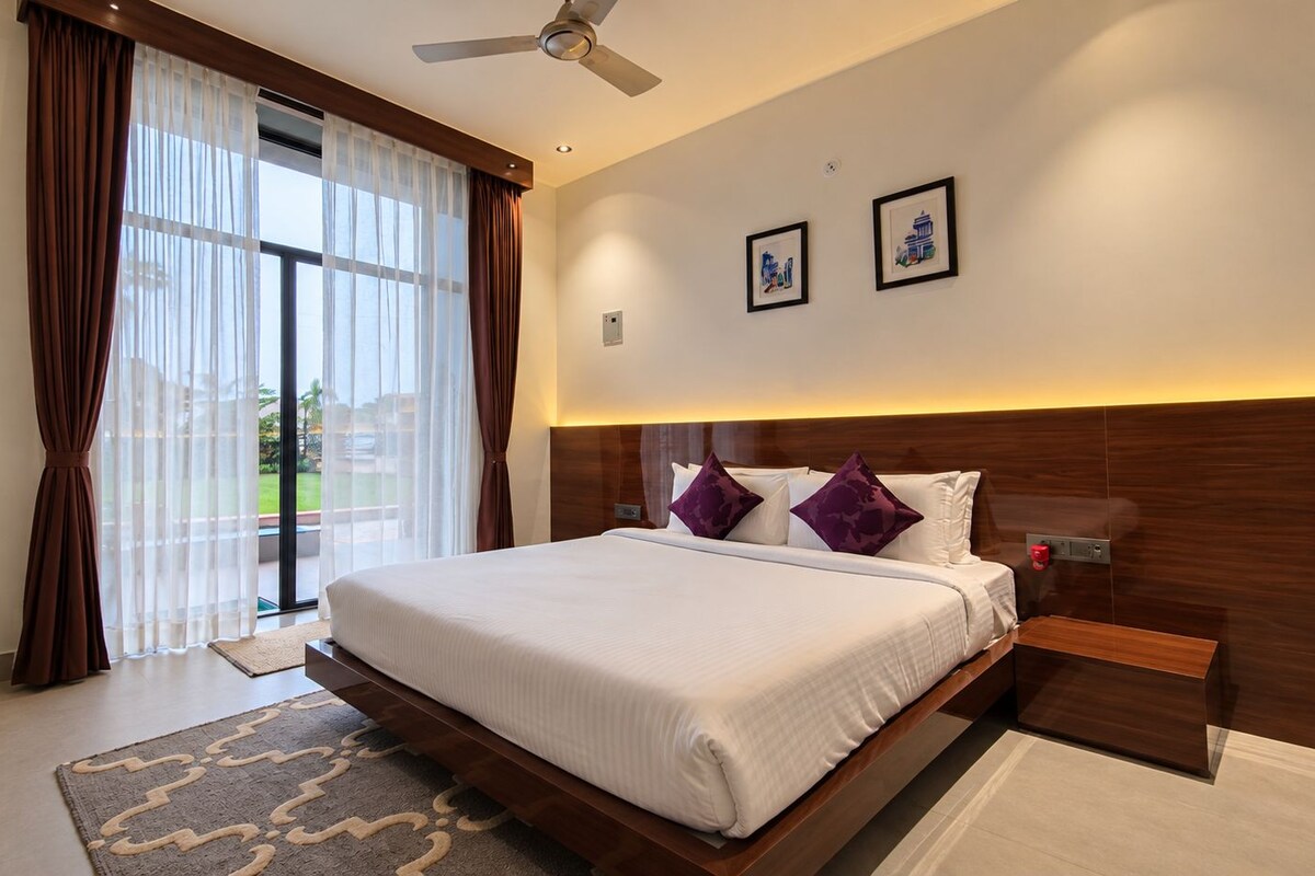 Quarto de hotel moderno com uma cama grande, ventilador de teto e vista para o exterior pela janela.