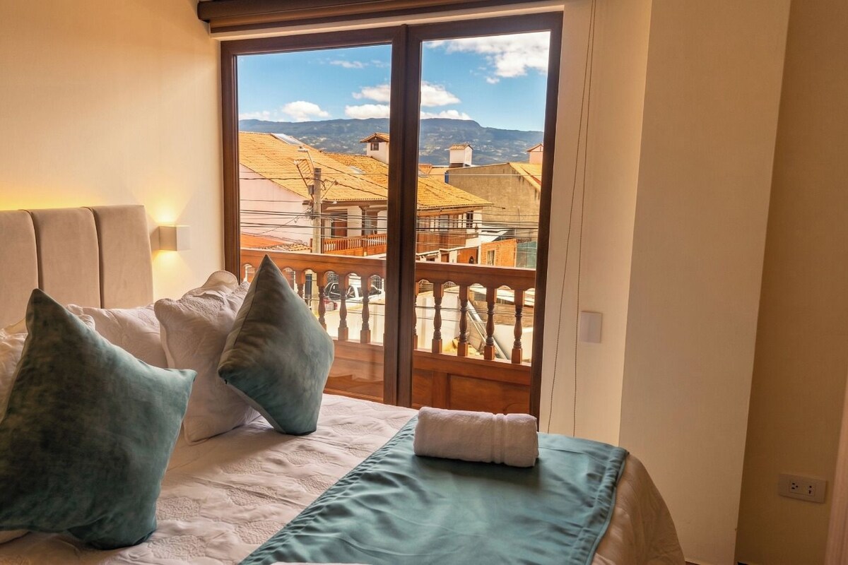 Quarto de hotel com cama, almofadas, vista para uma varanda e uma janela.