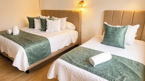 Duas camas de solteiro com cabeceiras, roupa de cama branca, mantas de lançamento verdes e almofadas combinando.