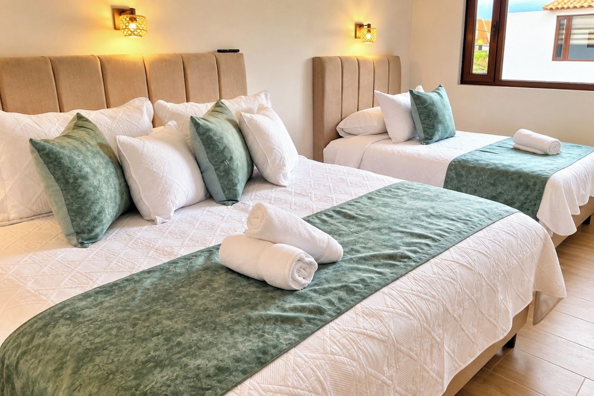 Duas camas de casal com cabeceiras, roupa de cama branca, almofadas decorativas verdes e piso de madeira.