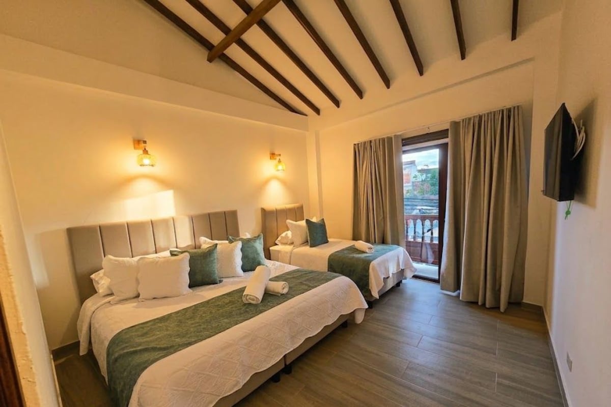 Quarto de hotel com duas camas, varanda e televisão na parede.