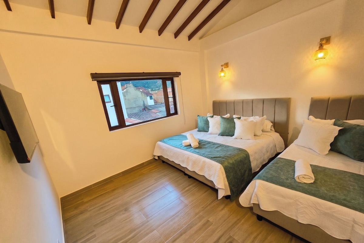 Quarto de hotel com duas camas, janela, soalho em madeira e televisão montada.
